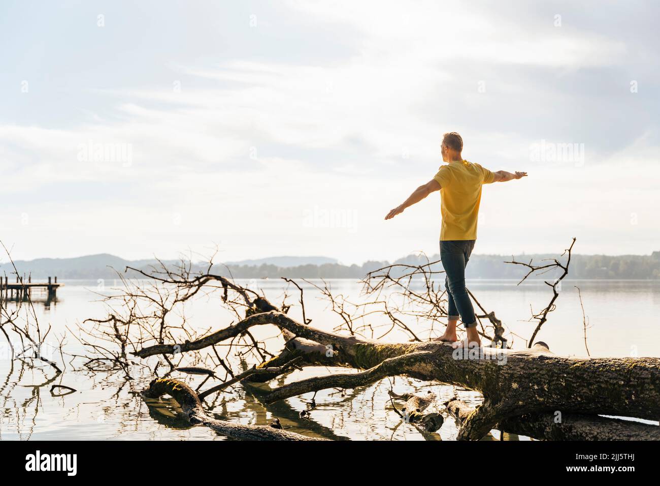 Man with arms outstretched walking on fallen tree at lake Stock Photo ...