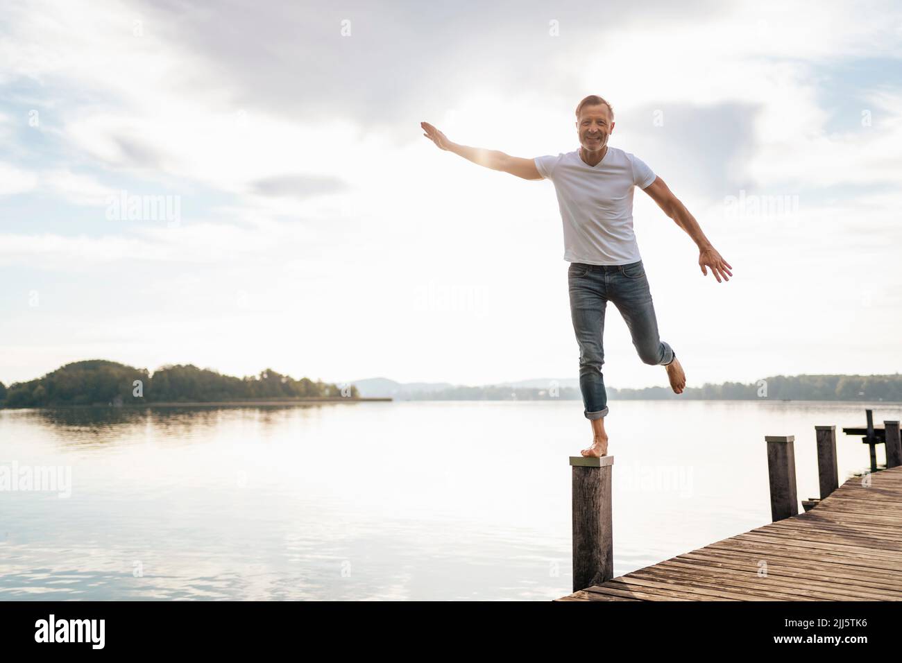 Happy mature man balancing on wooden post of pier Stock Photo - Alamy