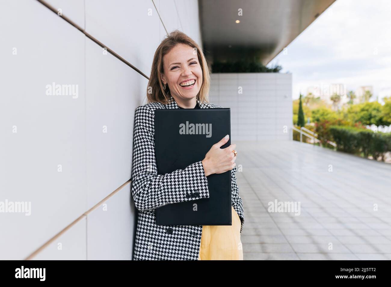 Happy businesswoman holding file folder leaning on wall Stock Photo - Alamy