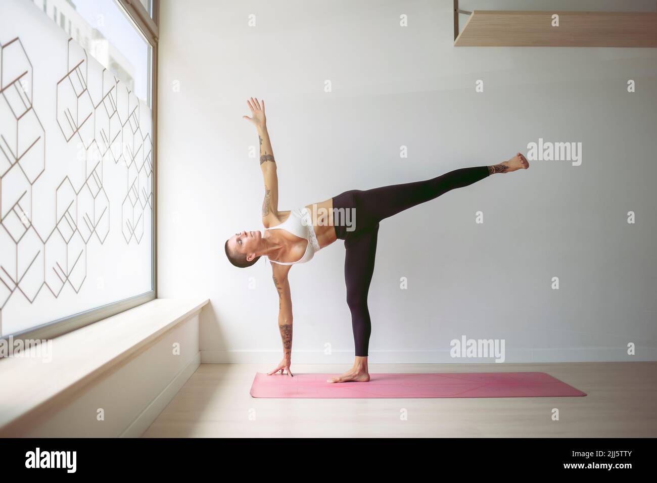 Woman balancing on exercise mat doing yoga in front of wall Stock Photo ...