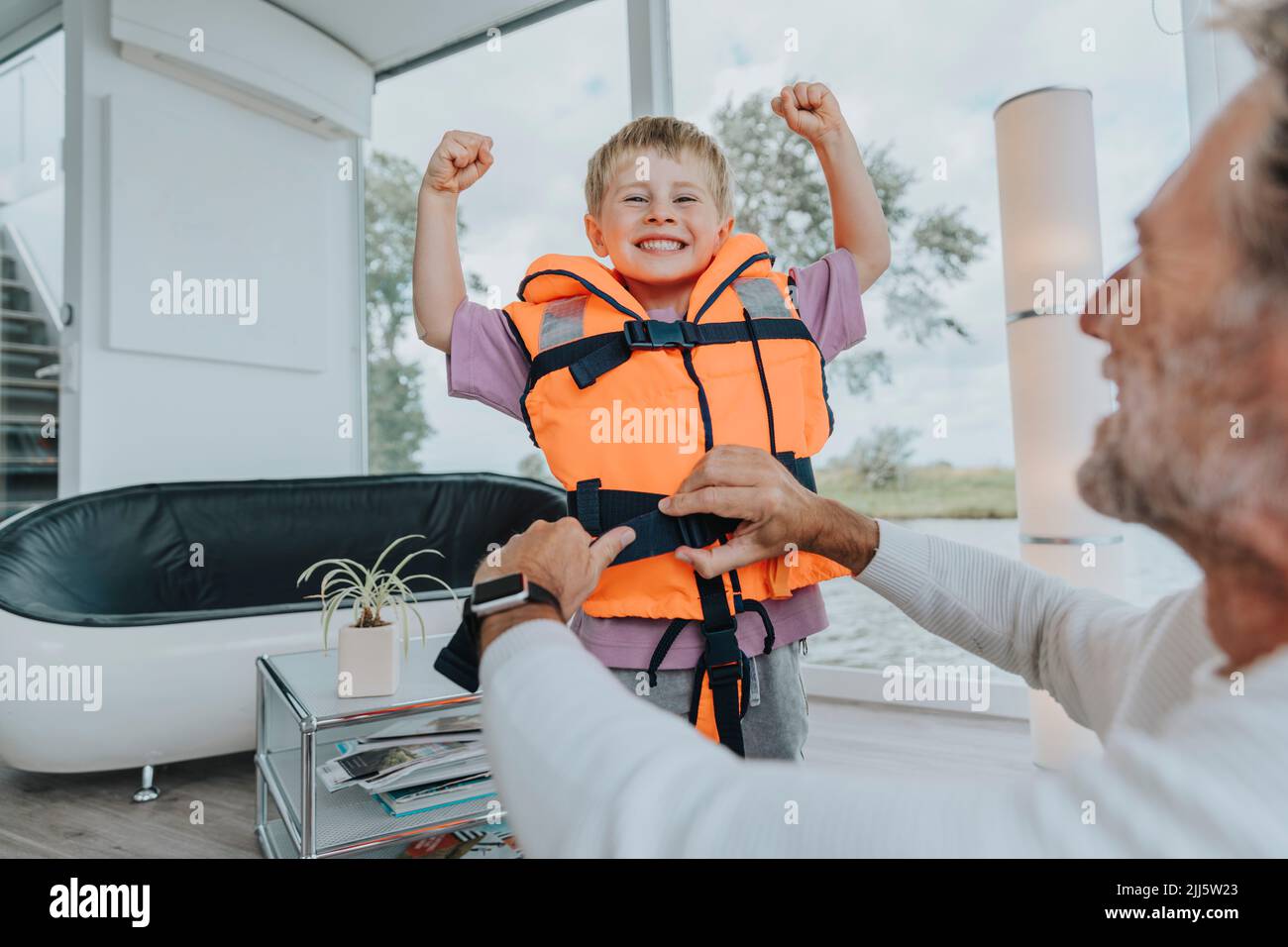 Happy son wearing life jacket flexing muscles at home Stock Photo - Alamy