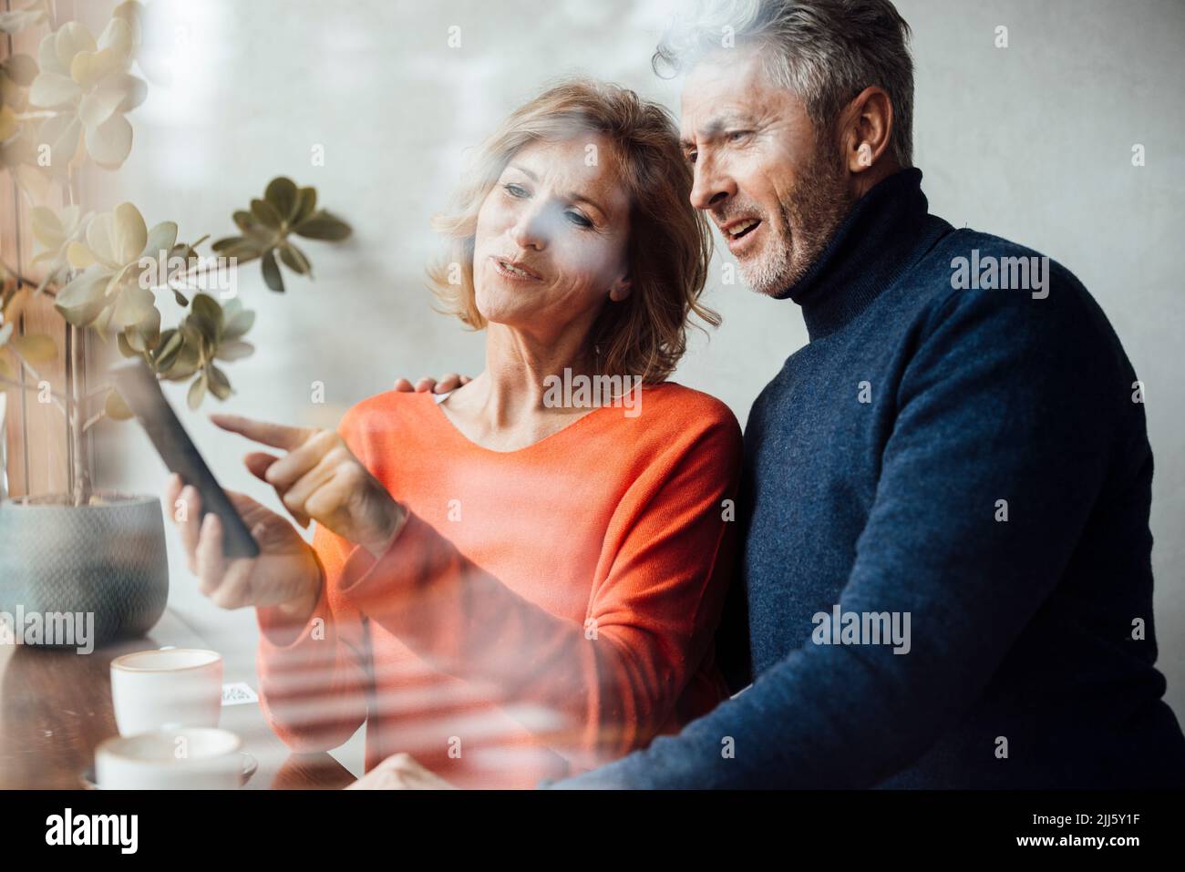 Woman sharing mobile phone with man in cafe seen through glass Stock ...