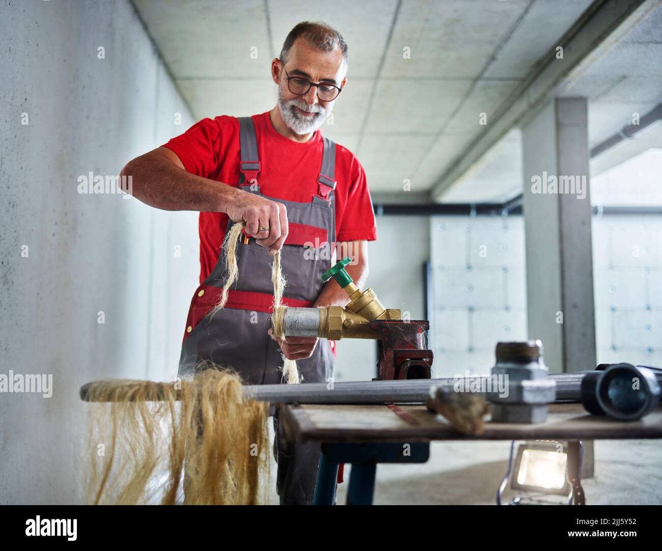 Plumber tying hemp gasket to metal pipe at workbench Stock Photo - Alamy