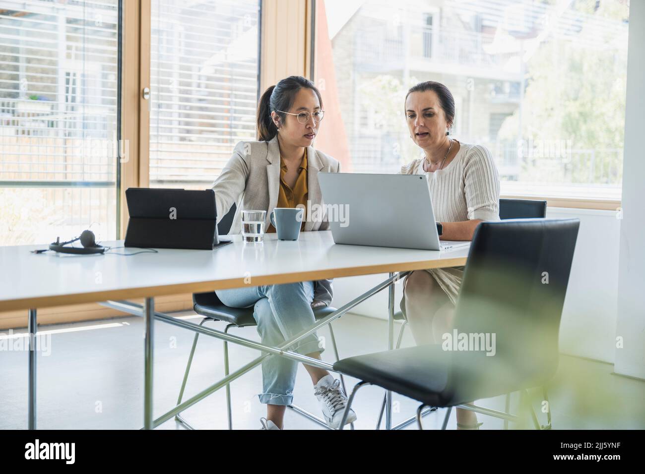 Mature businesswoman with colleague discussing over laptop in office ...
