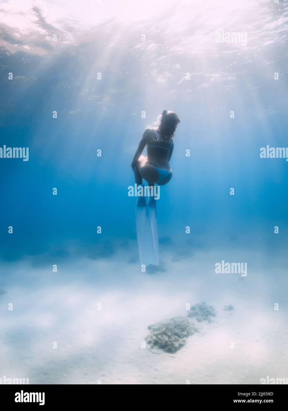 Woman freediver in bikini posing underwater over sandy sea bottom with ...