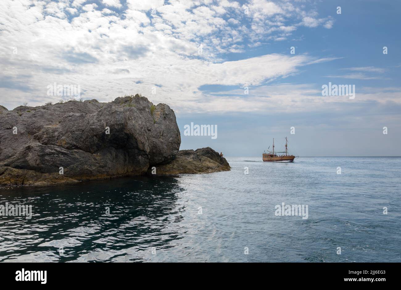 A sailing ship emerges from behind a rock jutting out into the sea ...