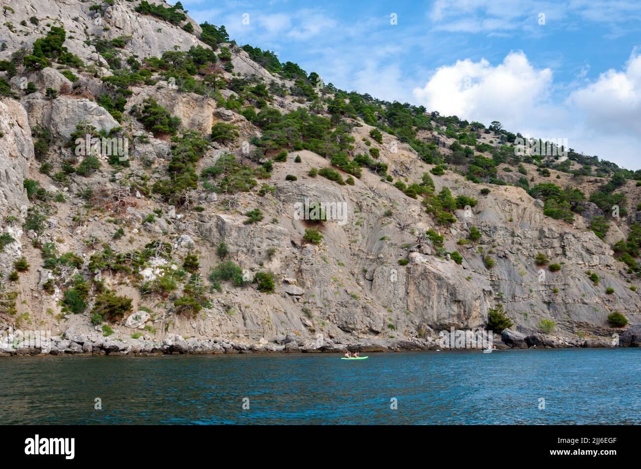 Rocky seashore, near which people swim in boats. Summer, sunny day ...