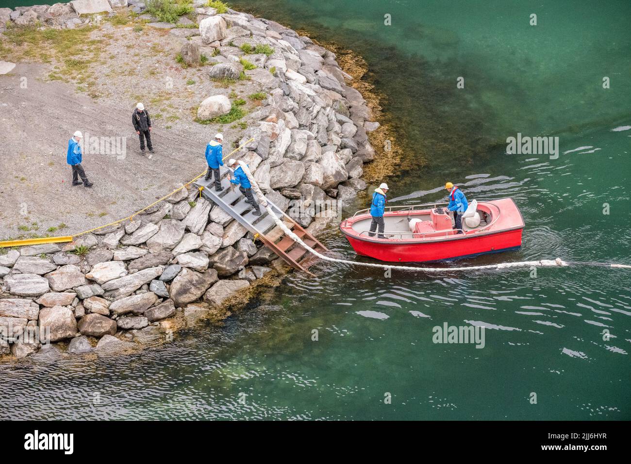 Norwegian harbour workman attaching mooring ropes to fixed mooring ...