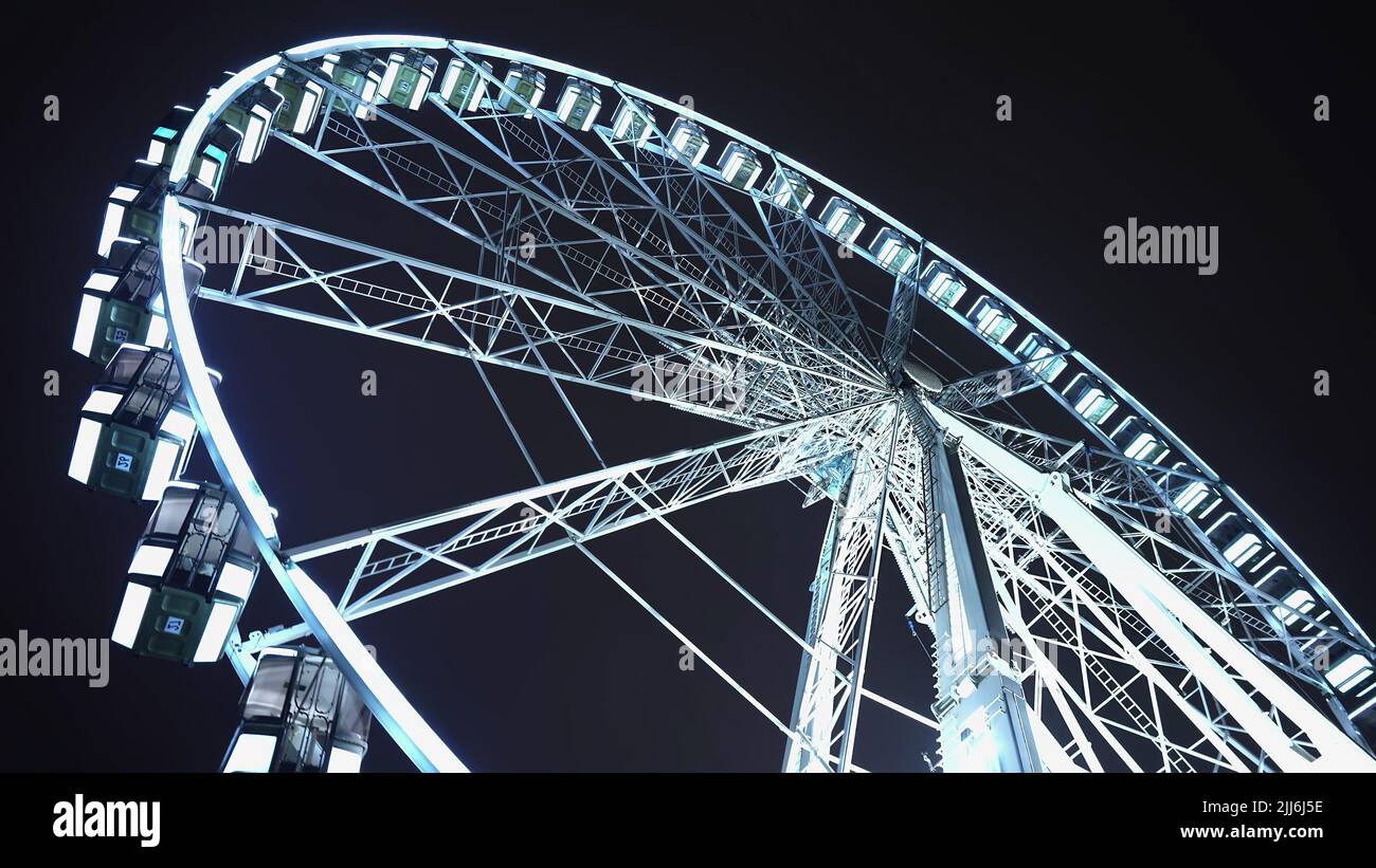 Brightly lit ferris wheel ride, which spinning at night or evening ...