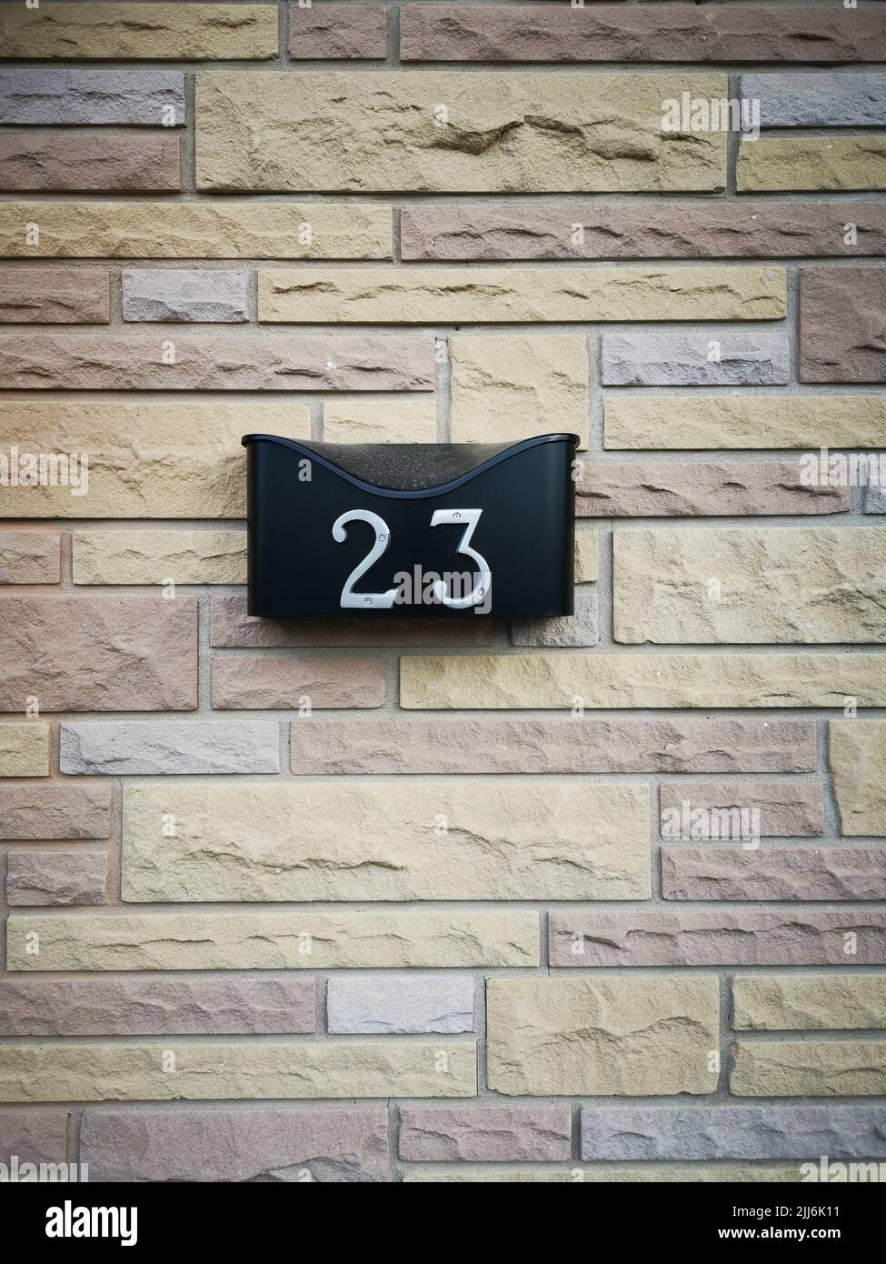 A vertical shot of a black sign for a house with the brick background ...