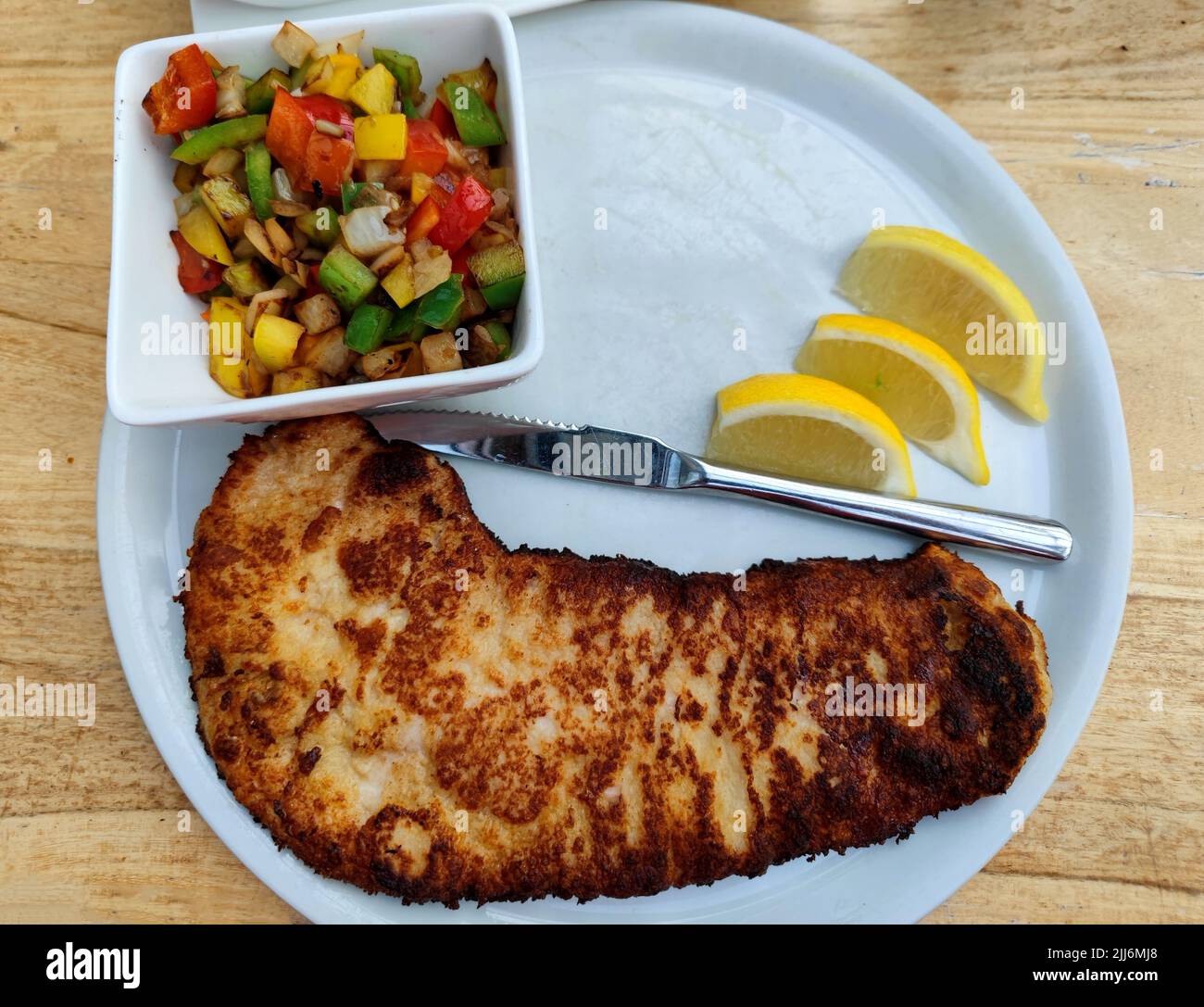Wiener schnitzel with a bowl of fried bell pepper and onion and three ...