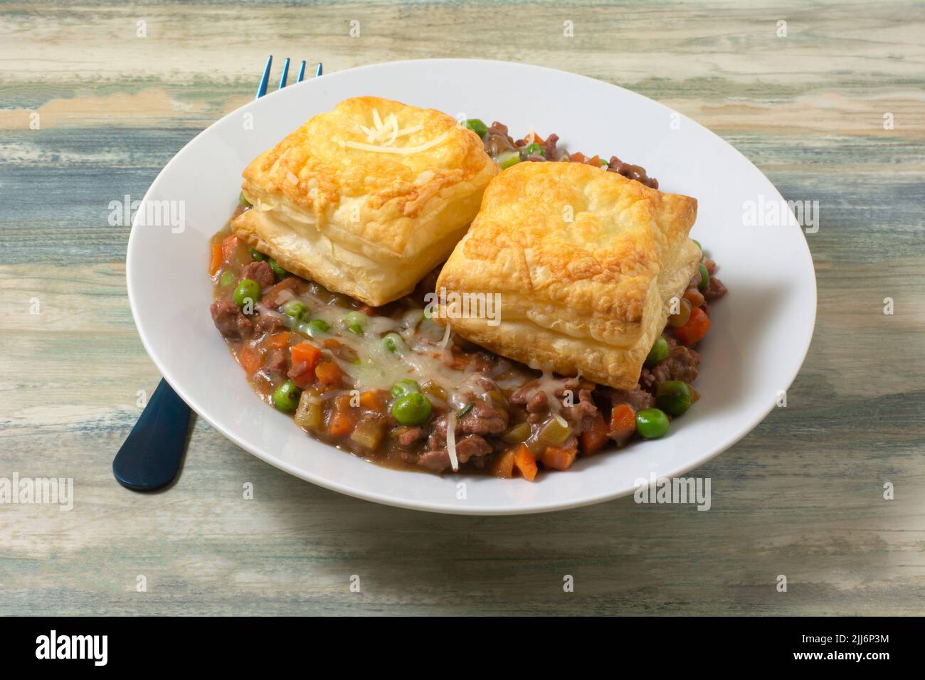 Beef and vegetable stew with puff pastry in white bowl with blue fork ...