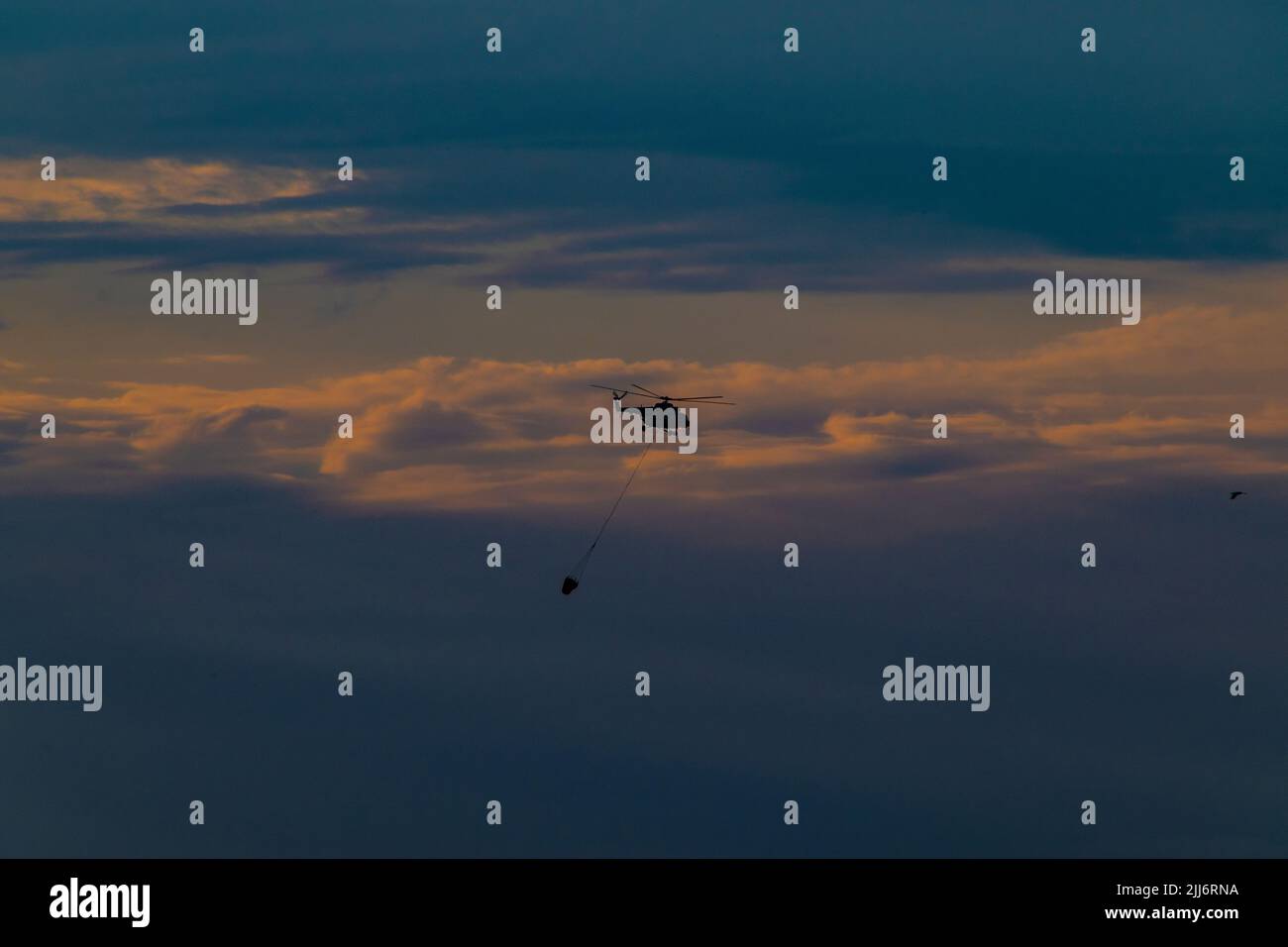 A helicopter carrying a package flying in a sunset sky Stock Photo - Alamy