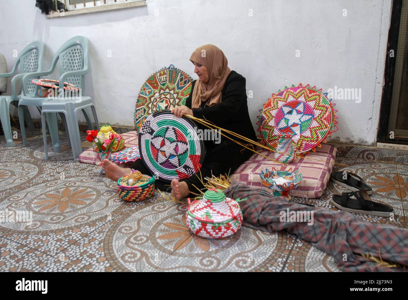 An elderly lady weaves crafts from straw to be sold at the Palestinian ...
