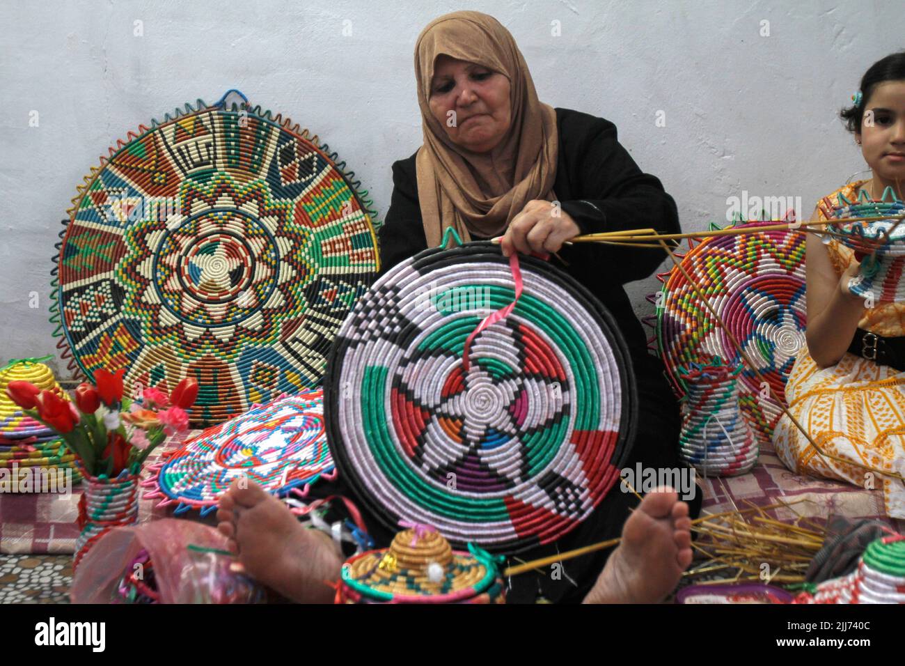 An elderly lady weaves crafts from straw to be sold at the Palestinian ...