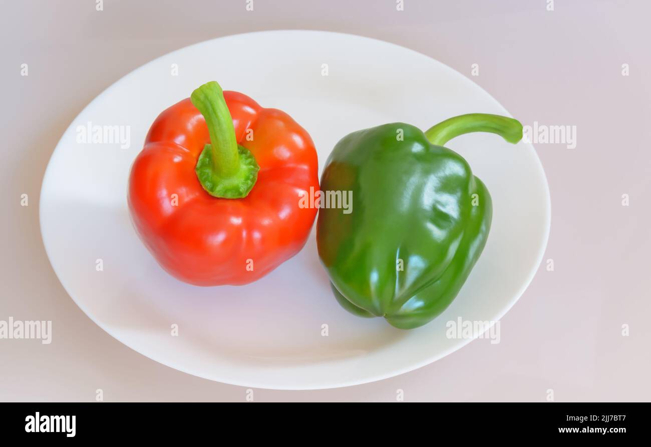 Two sweet peppers, green and red on a white plate Stock Photo - Alamy