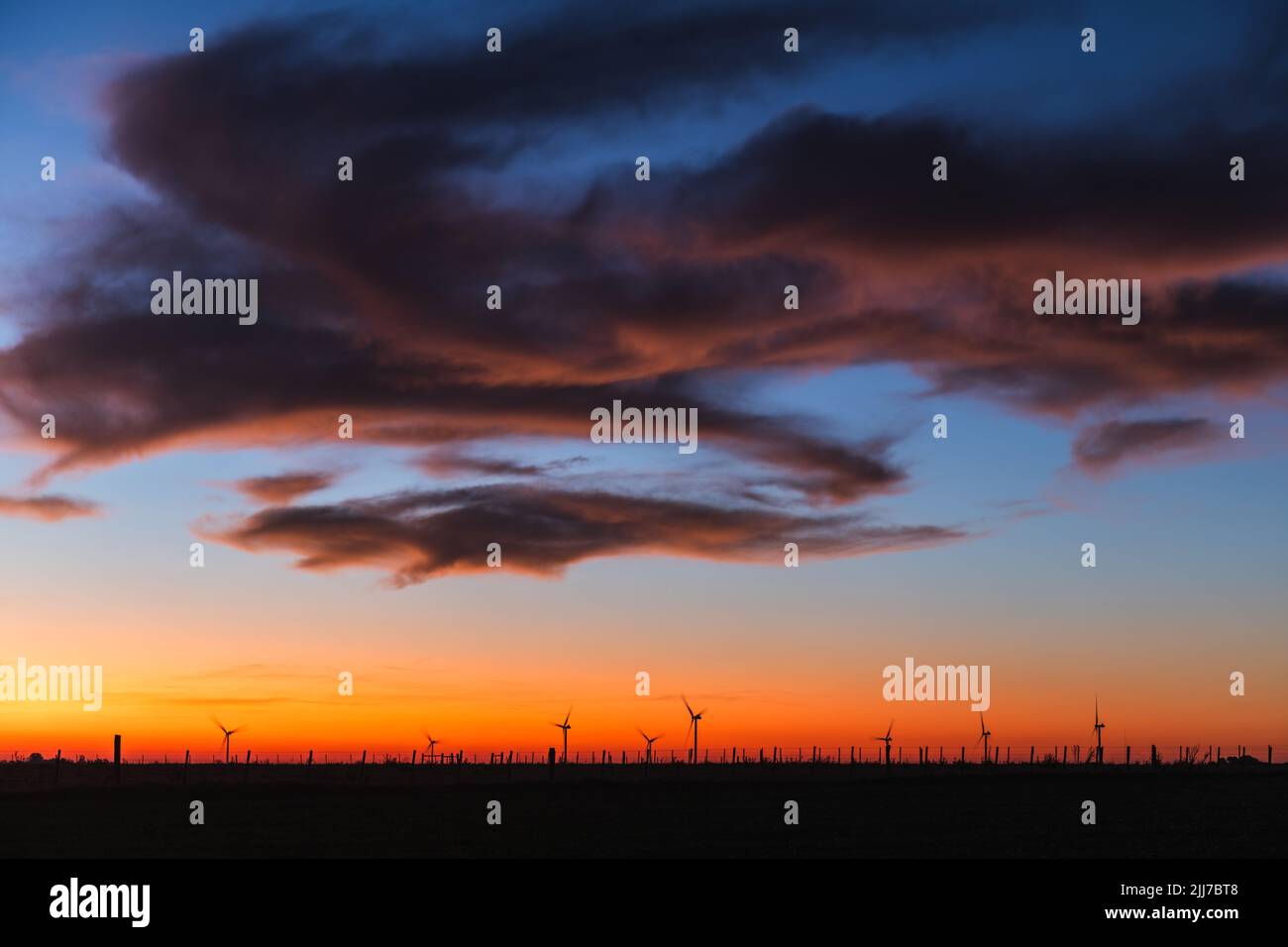 Silhouette of a set of modern windmills under a reddish sunset, with a ...