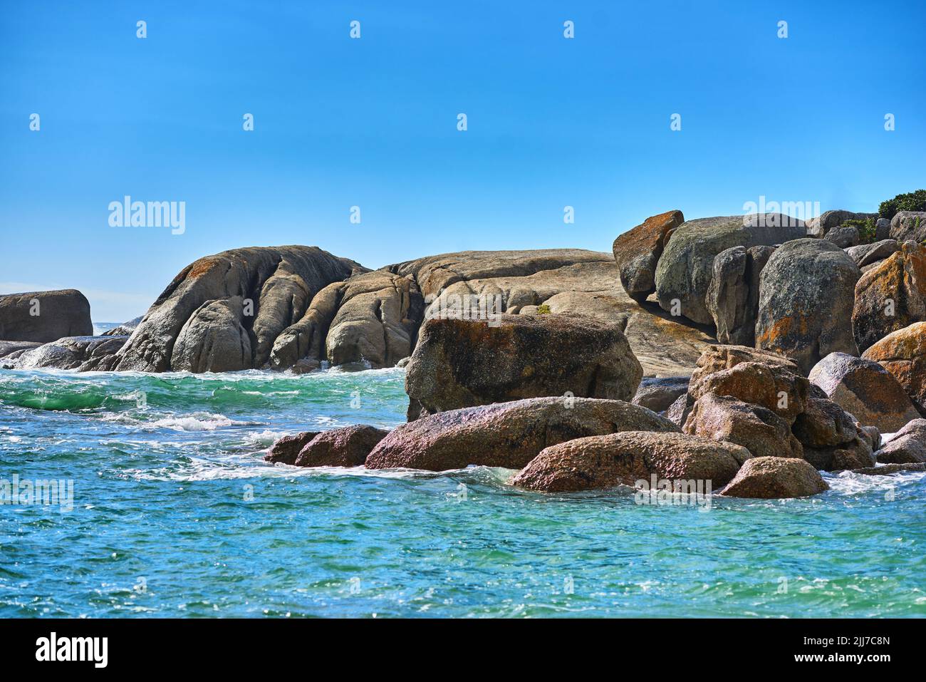 Boulders or big rocks in a calm ocean against a clear blue sky ...