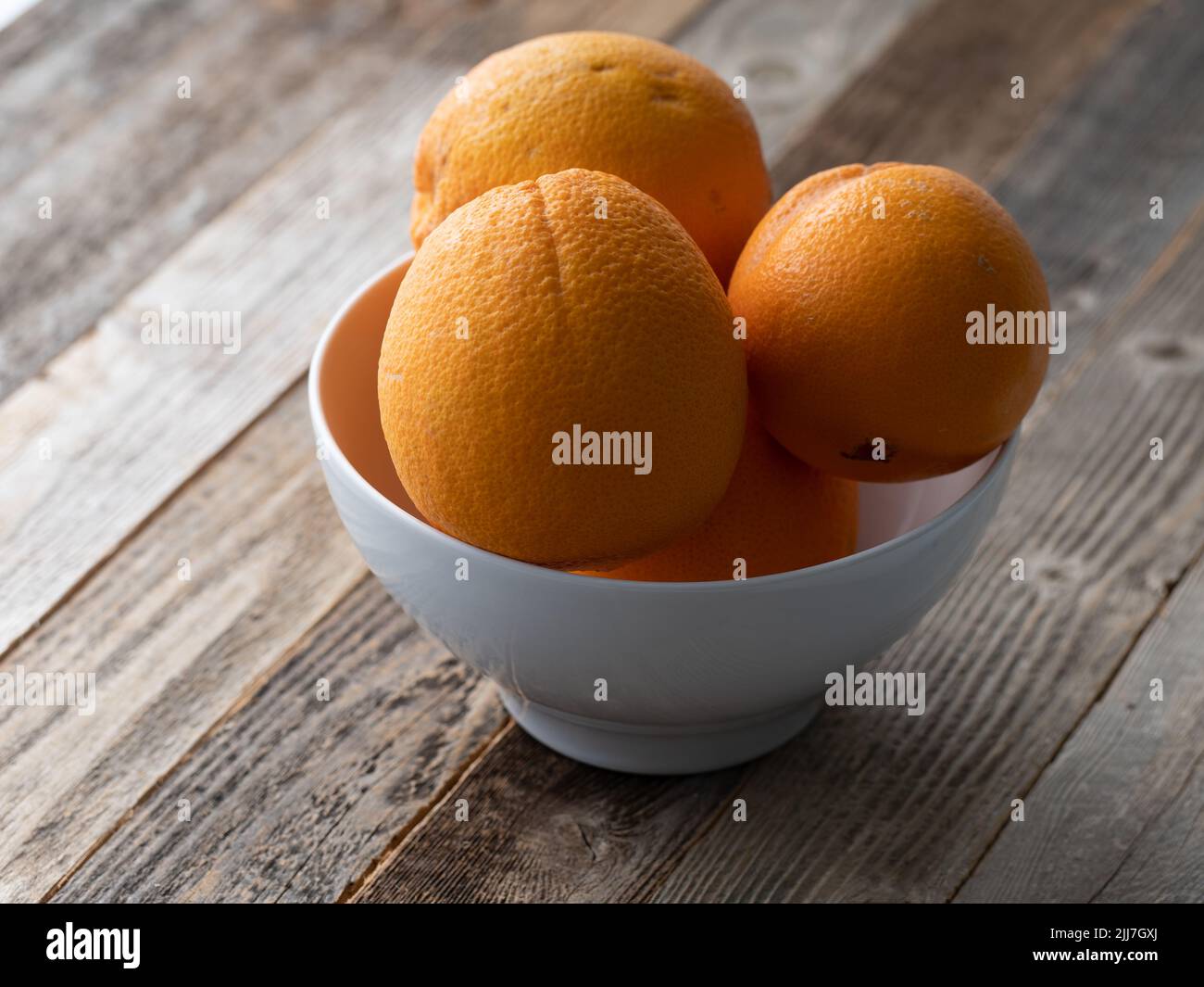 White bowl overflowing with navel oranges on wood table Stock Photo - Alamy