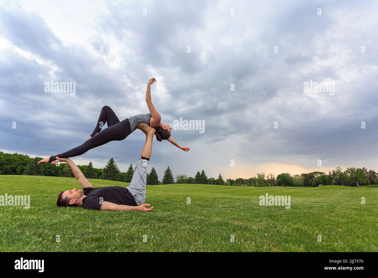 Healthy man lying on grass and balancing woman. Couple doing acrobatic ...