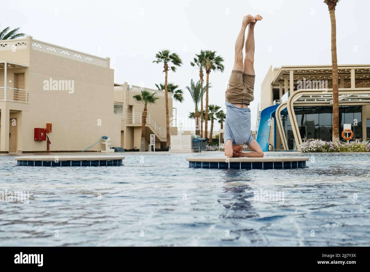 Man practicing yoga on the pier of swimming pool on resort over palm ...