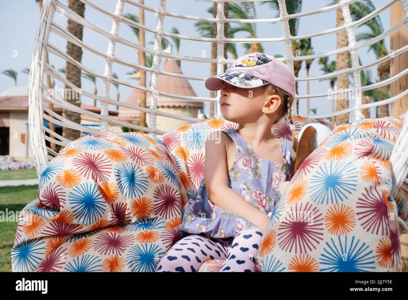Serious toddler girl on the swing. Stylish and moody child having rest ...