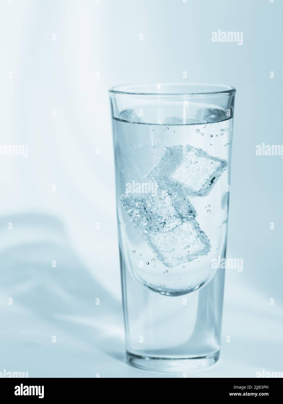 Glass of clean mineral sparkling water with ice on light blue ...