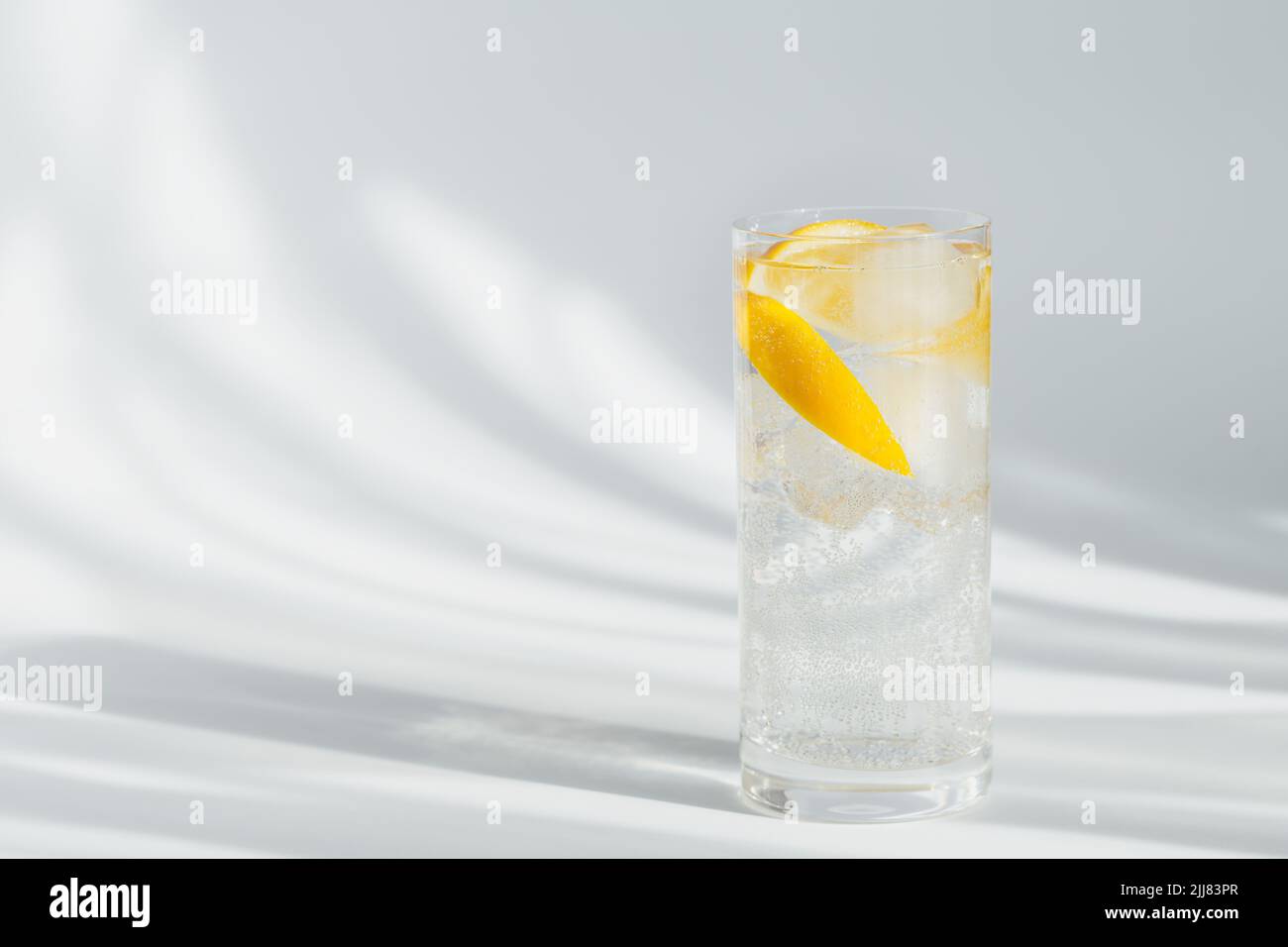 Glass of clean mineral sparkling water with ice and lemon on a white background with sunshine ...