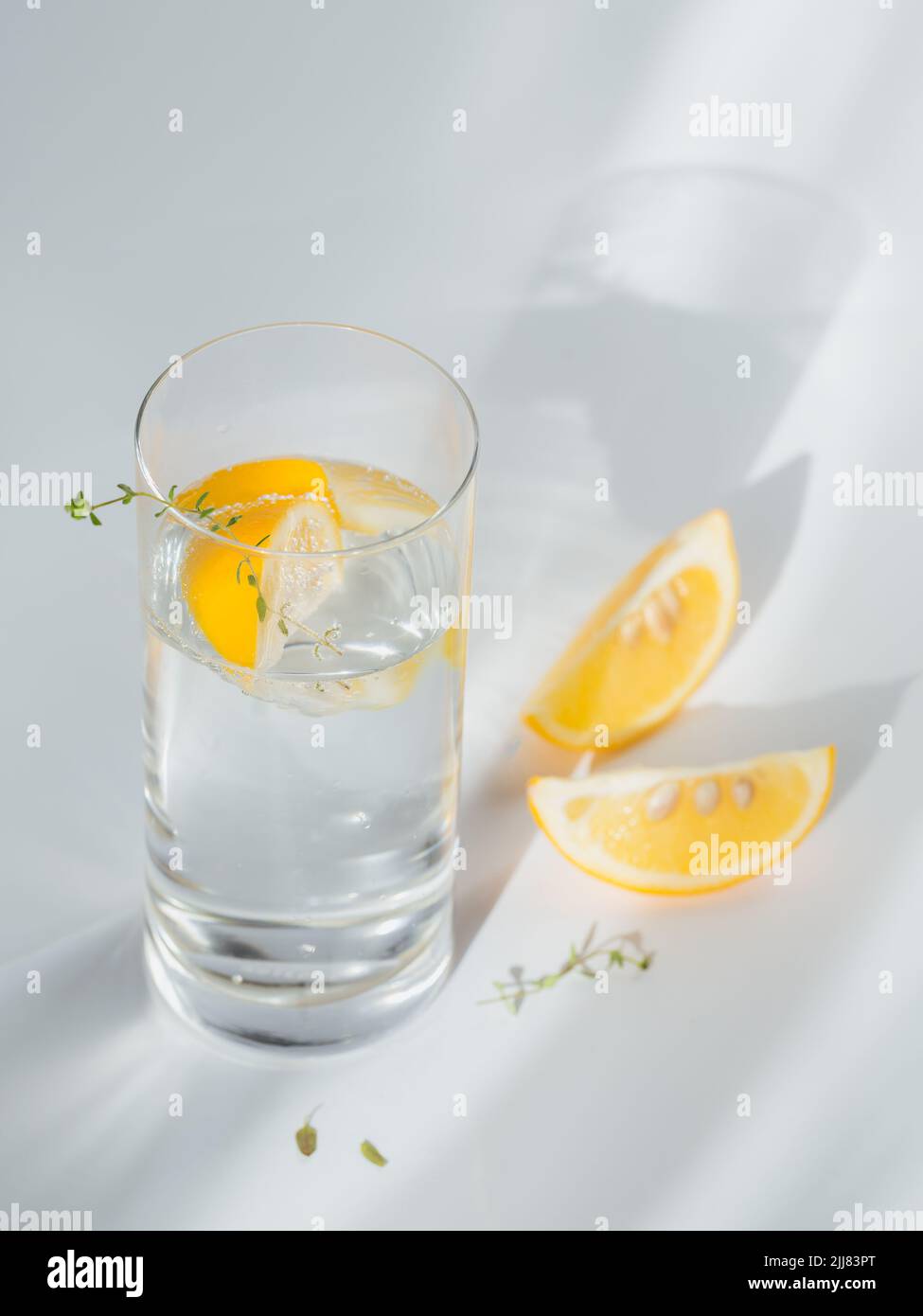Glass of clean mineral sparkling water with ice and lemon on a white background with sunshine ...