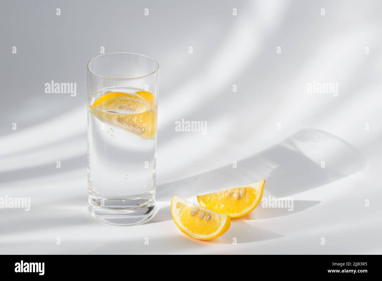 Glass of clean mineral sparkling water with ice and lemon on a white background with sunshine ...