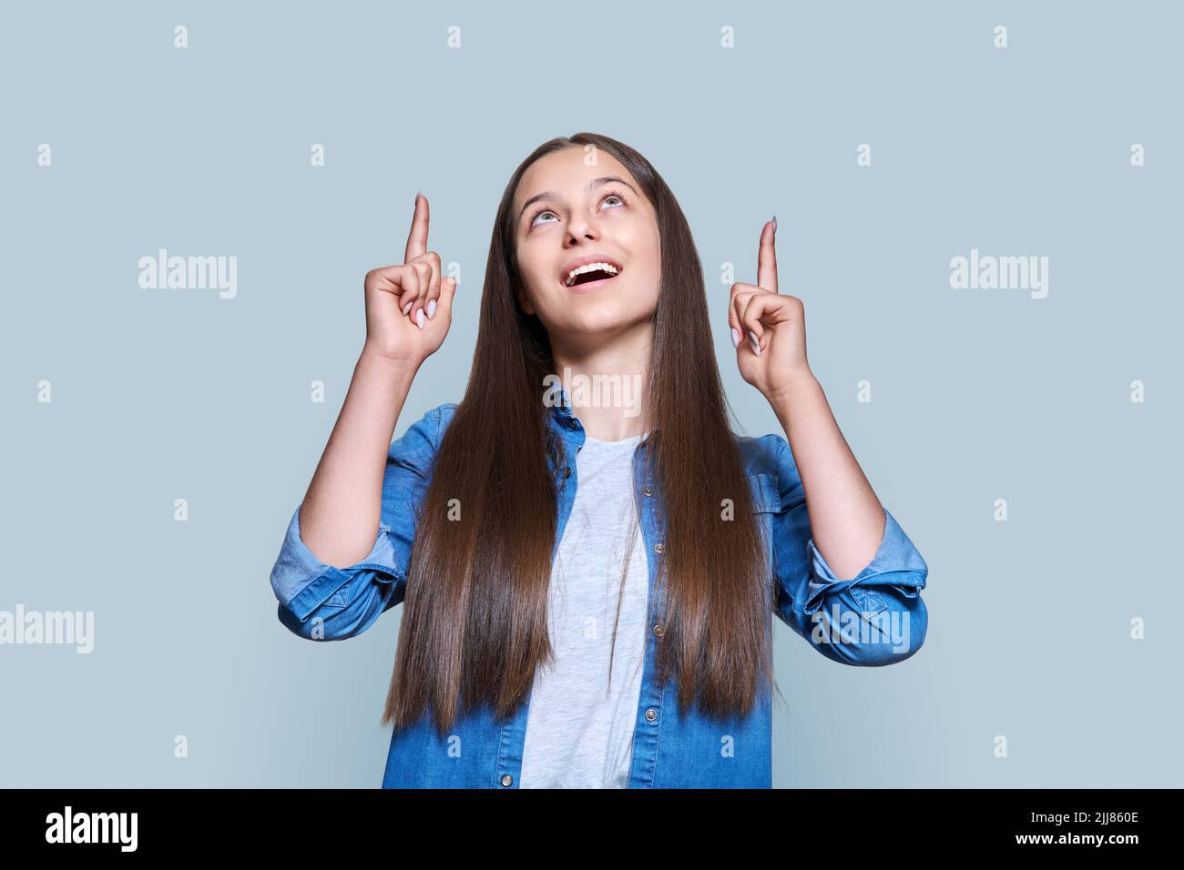 Teenage girl pointing fingers up at the place for text, on gray ...