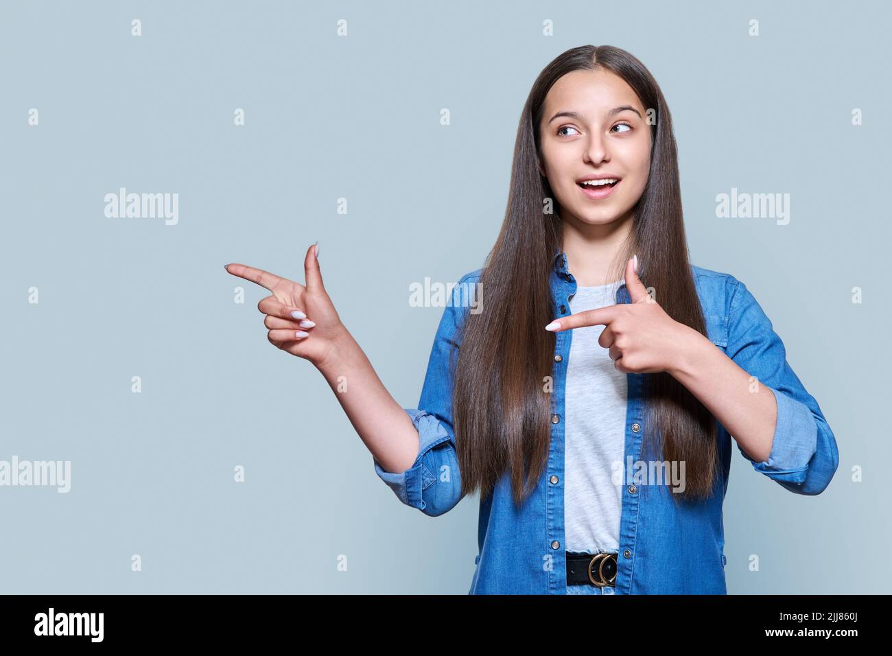 Teenage girl pointing fingers to the side at space for text, on gray ...
