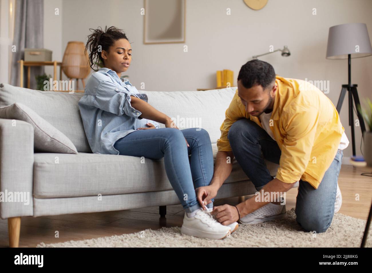 Black Husband Caring For Pregnant Wife Lacing Her Shoes Indoor Stock
