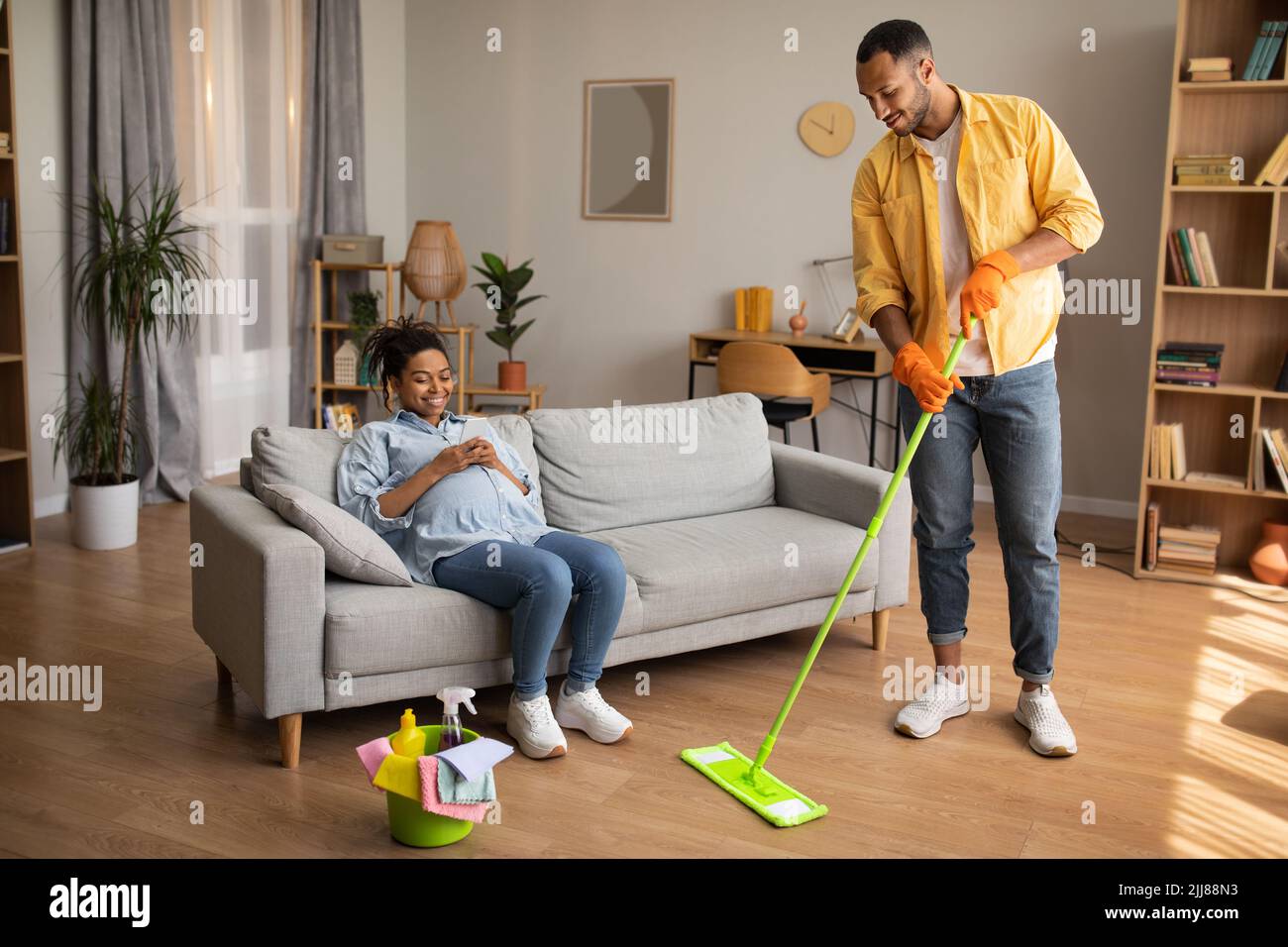 Black Husband Doing House Chores While Pregnant Wife Resting Indoor