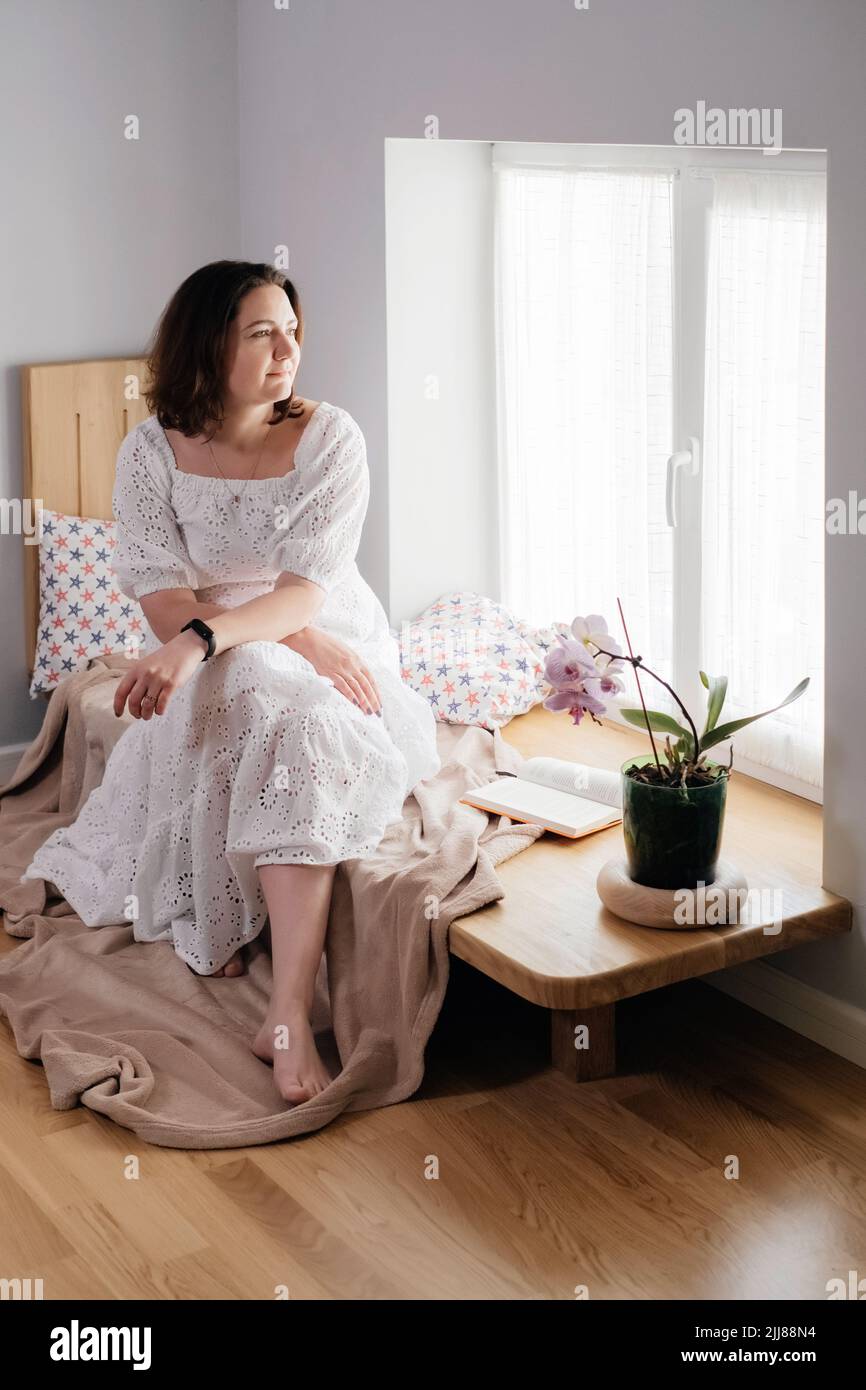 Mid age adult woman plus size reading a book looking at the window on ...