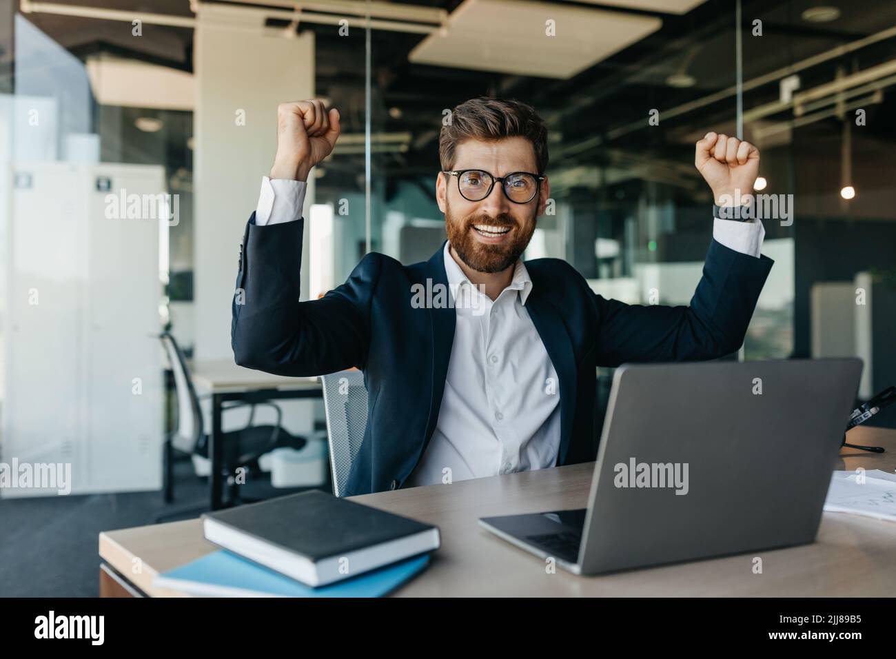Emotional businessman gesturing yes and shaking fists, sitting at ...