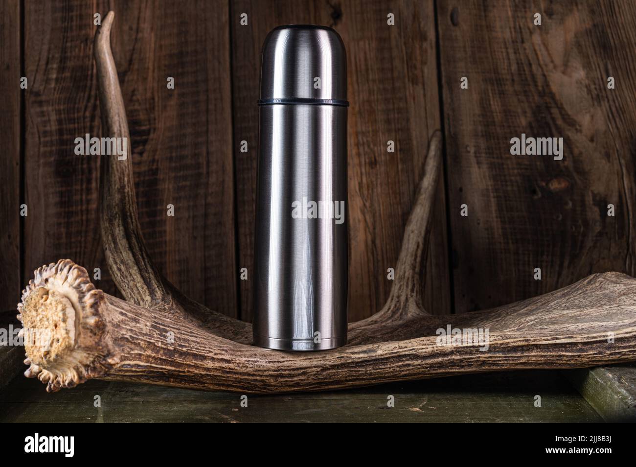 Steel shiny thermos on a wooden background. Thermos on the horn of an ...
