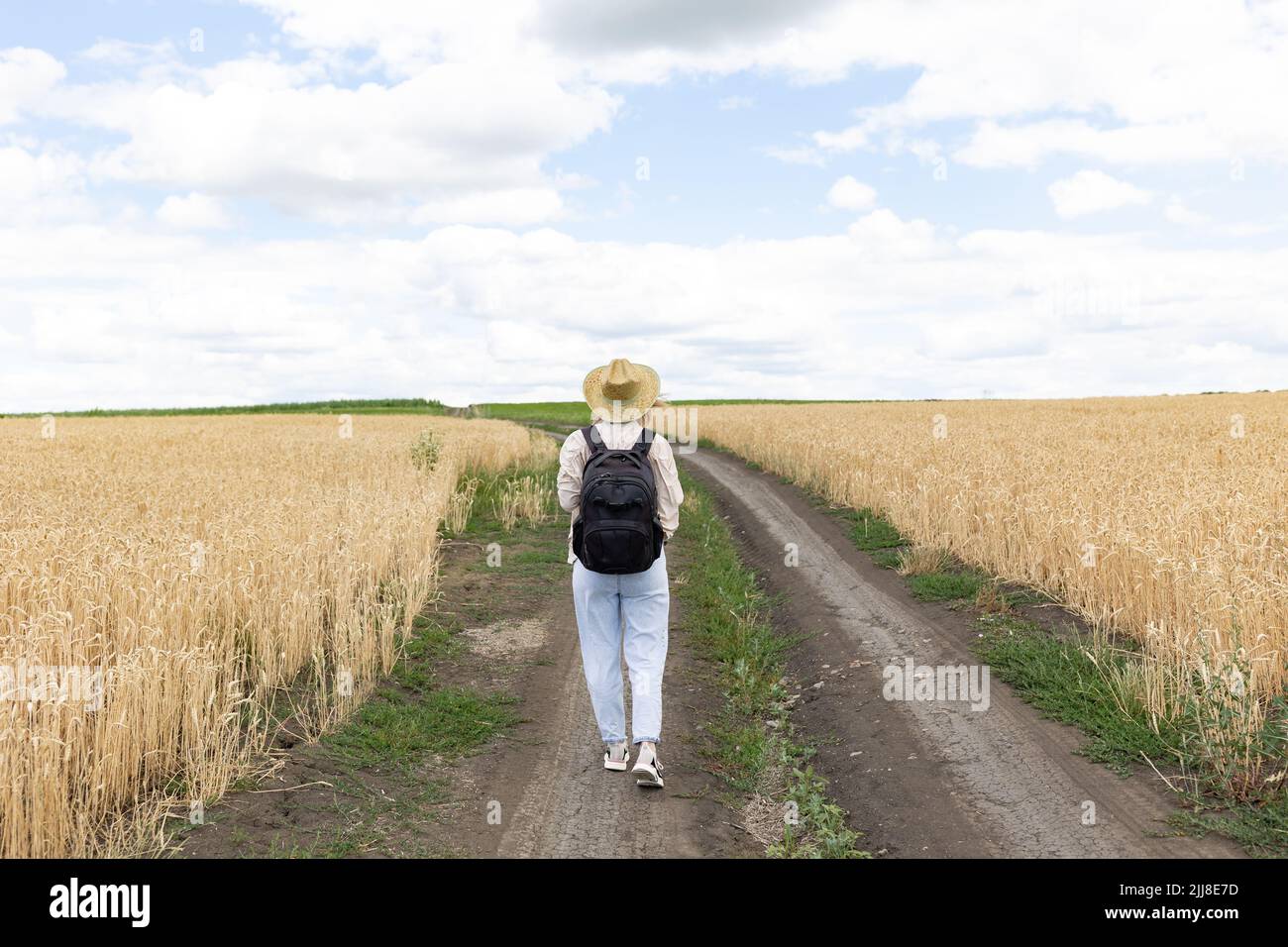 woman tourist in a hat with a backpack walking along the road past the ...