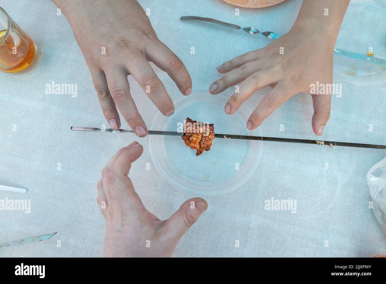 the last juicy piece of meat on a skewer, to which people's hands are ...