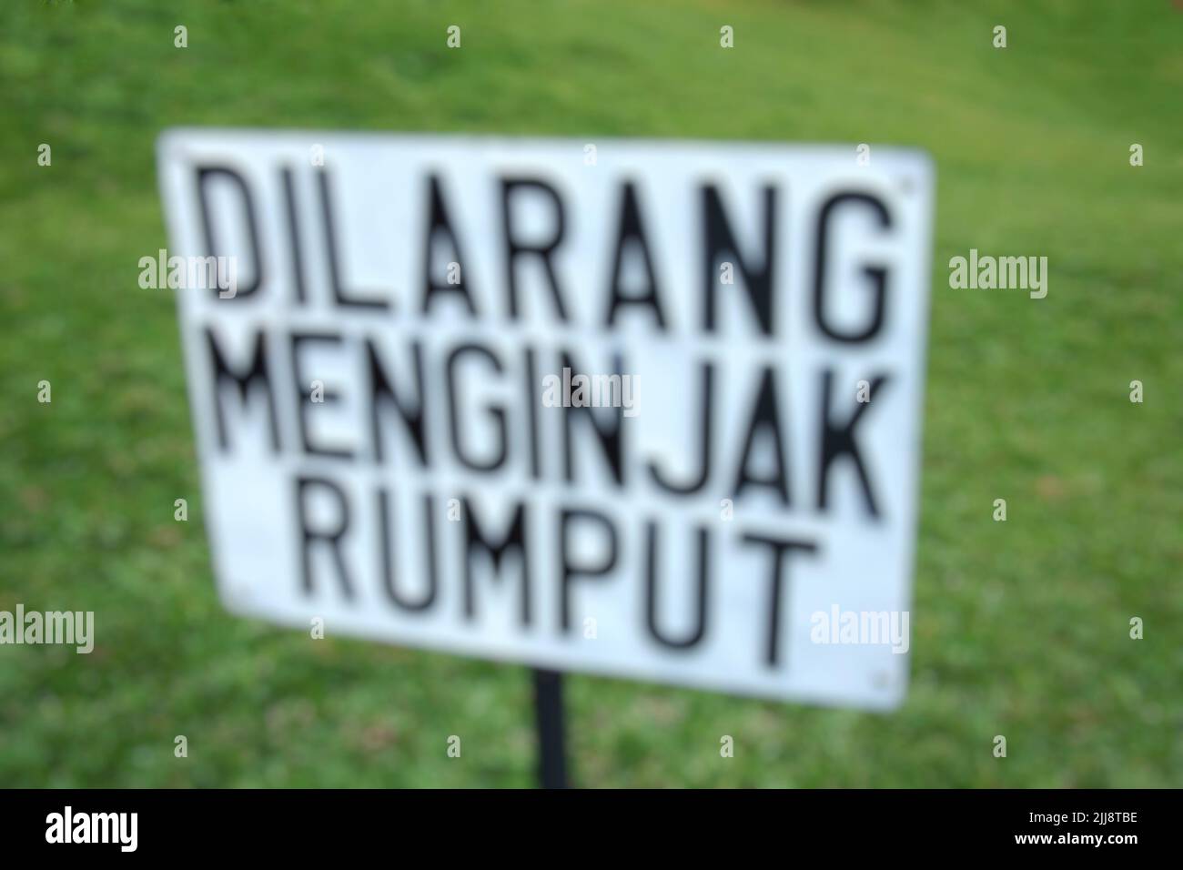 Blurred close up view of white warning sign board in green field which ...
