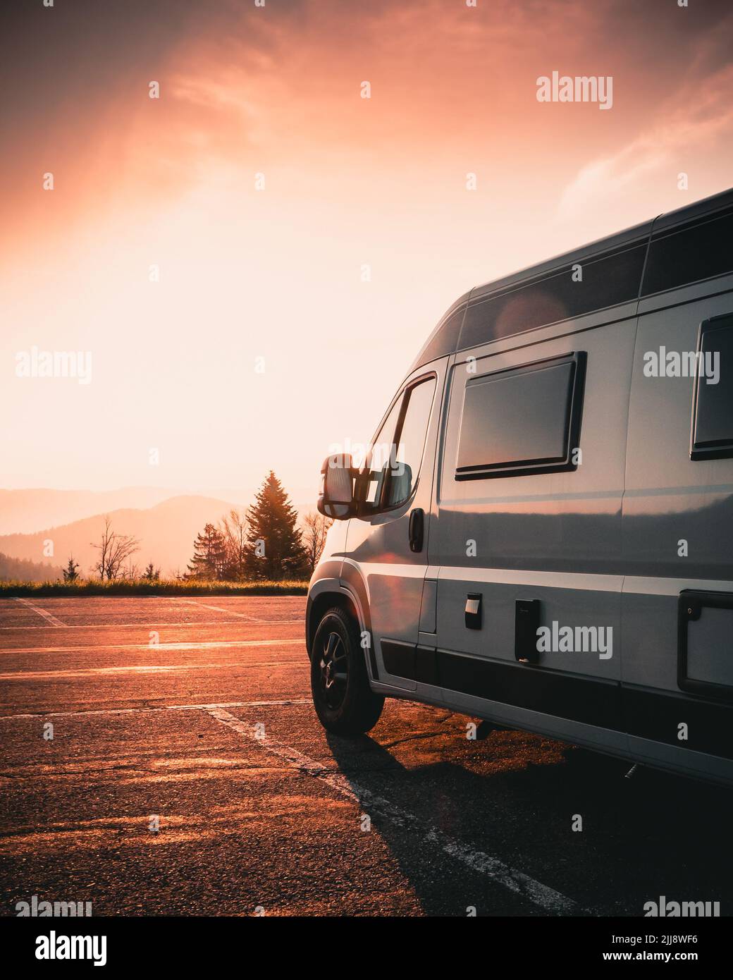 A campervan parked on the side of the road against a scenic sunset ...