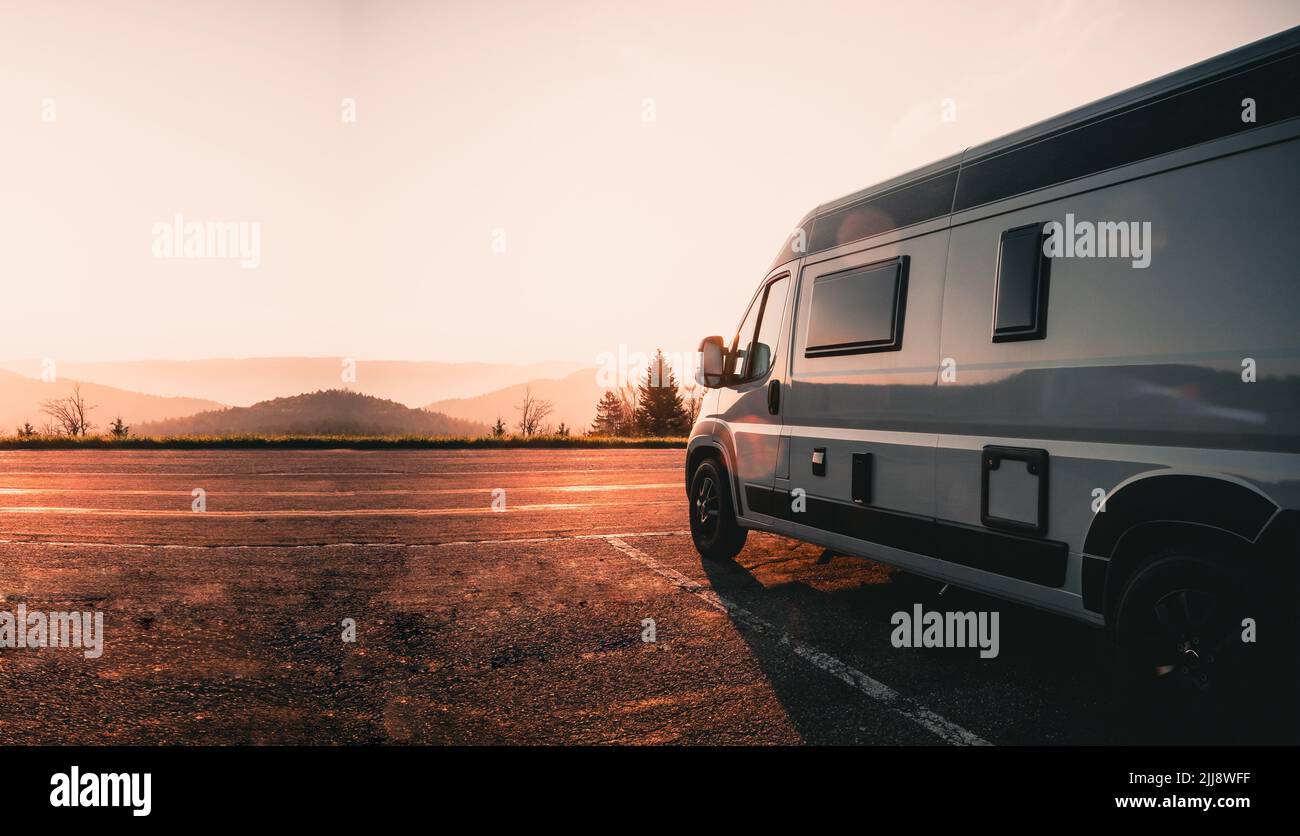 A campervan parked on the side of the road against a scenic sunset ...