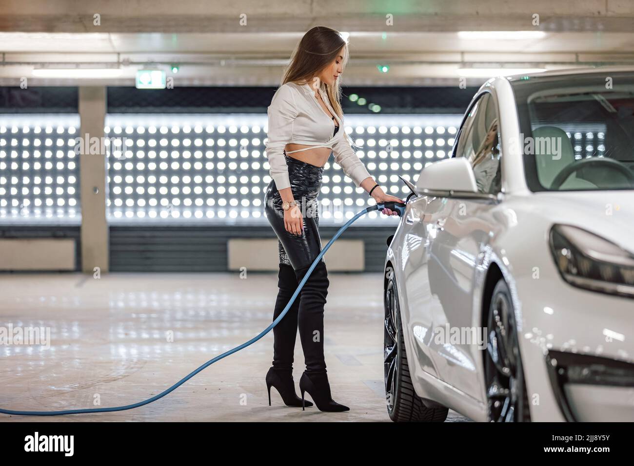Attractive young woman charging a luxury electric car at an electric ...