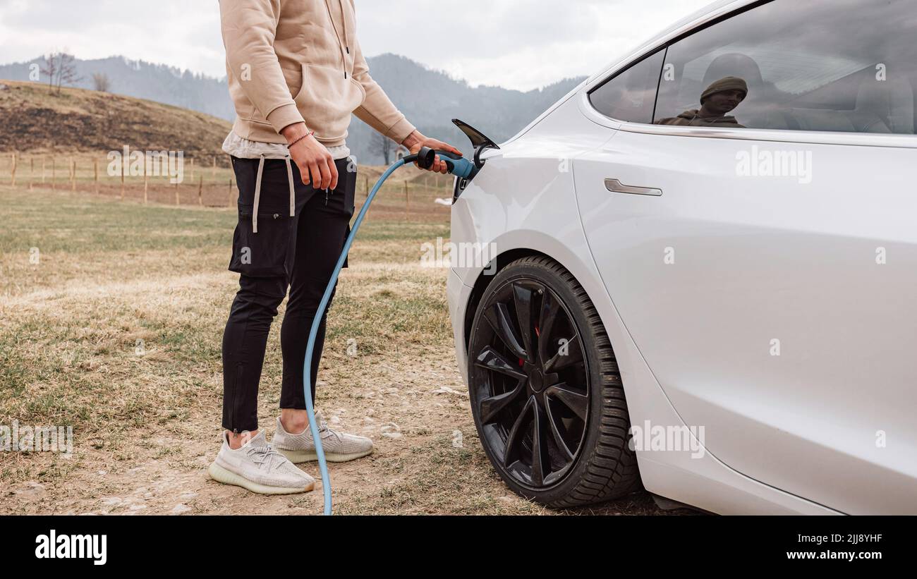 Male hand putting a charger in electric car socket, in the background ...