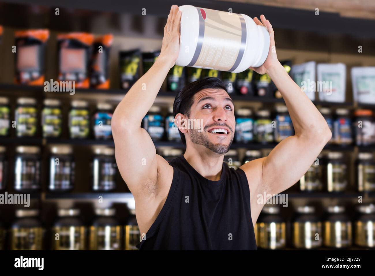 Young man bodybuilder holding big pot of sport nutrition over head ...
