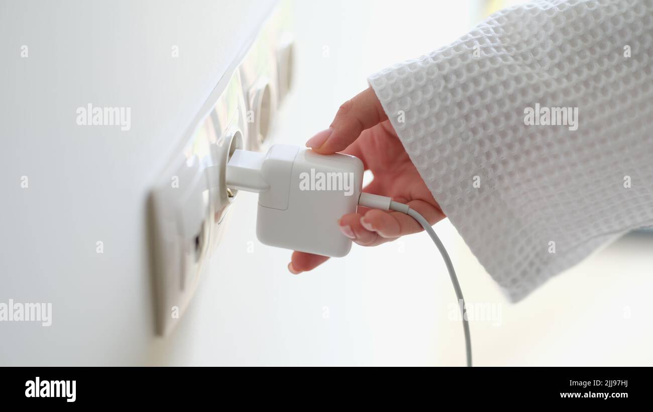 Woman hand in robe gown inserts white charger into socket in hotel ...