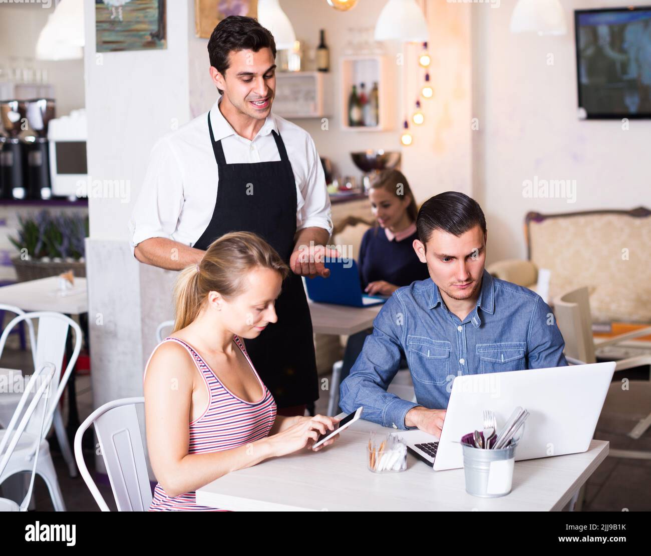 Positive waiter is greeting visitors and taking order Stock Photo - Alamy