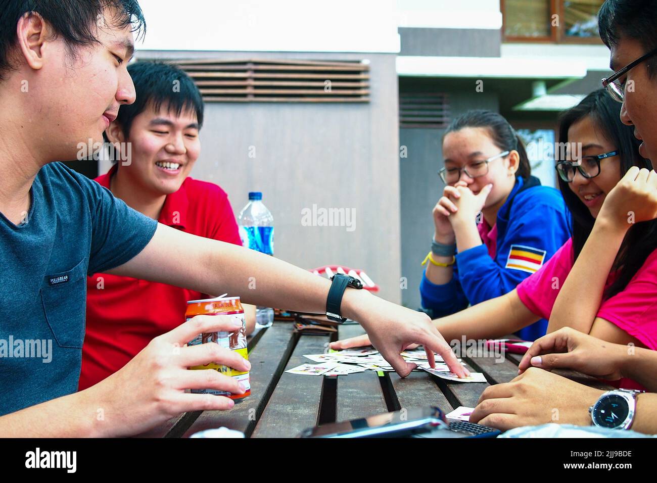 Group of young Asian people playing cards game on table wearing casual outfit. Smiling and fun ...