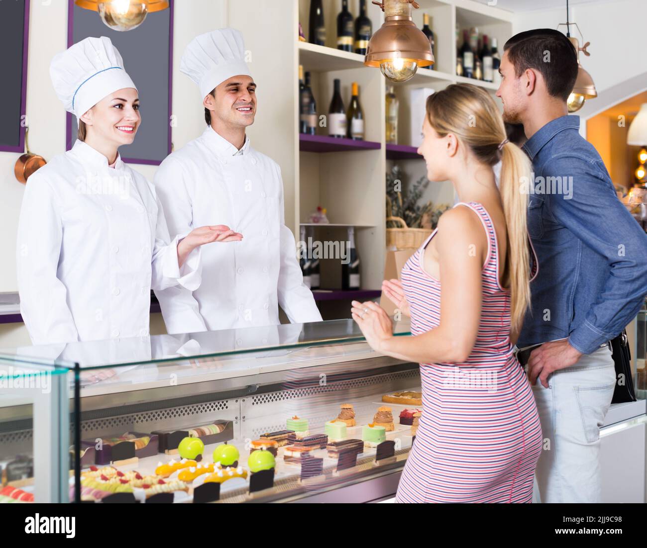 Two pastry chefs warmly greeting couple Stock Photo - Alamy