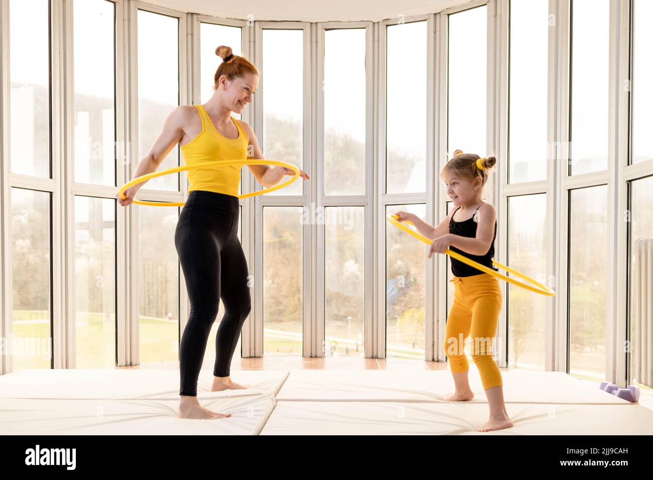 Young fit mom and her daughter having fun with hula hoop in a gym Stock ...